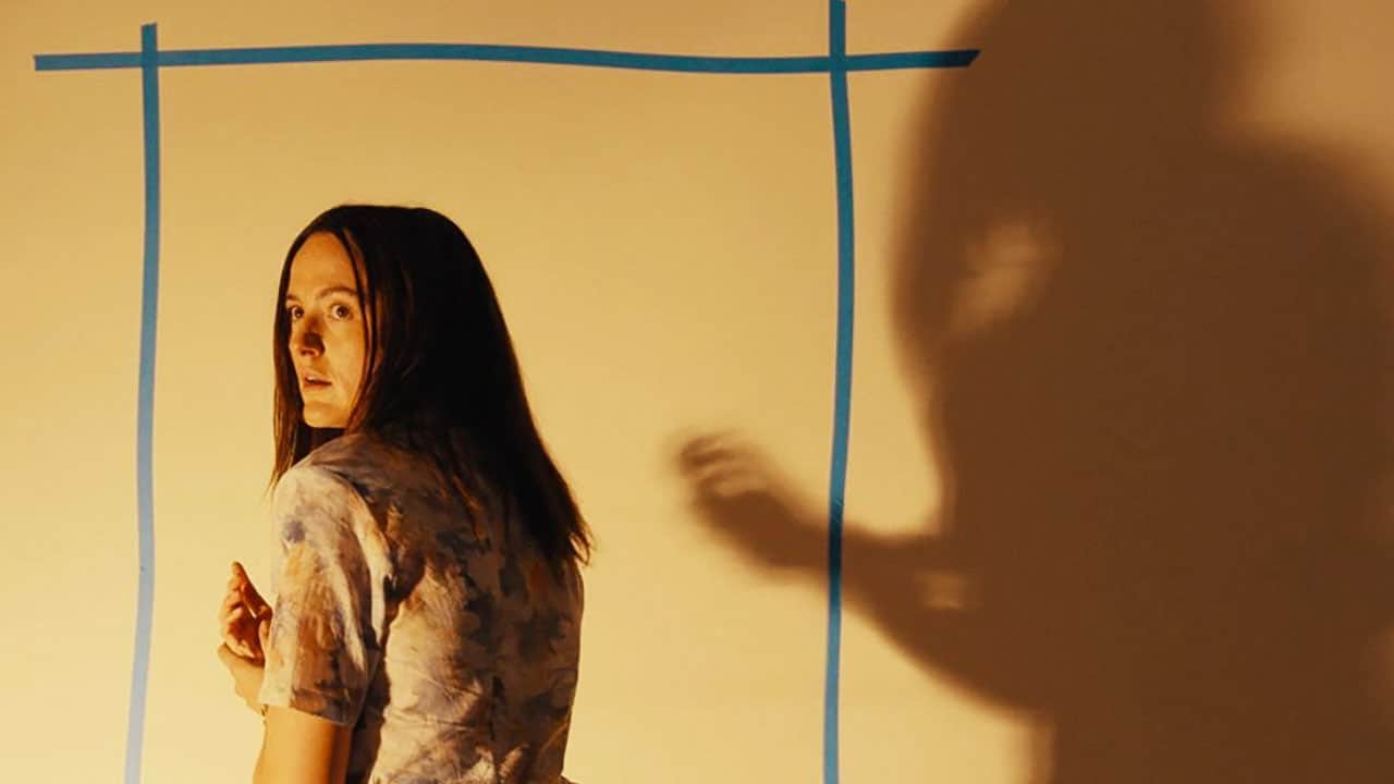A woman stands in front of a pale yellow wall with blue tapes in the ...